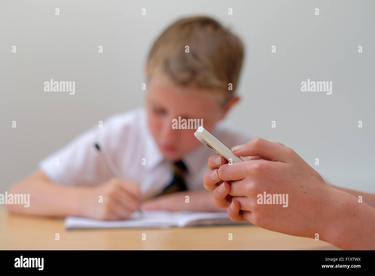 A school pupil using a mobile phone (texting) in class as another pupil ...