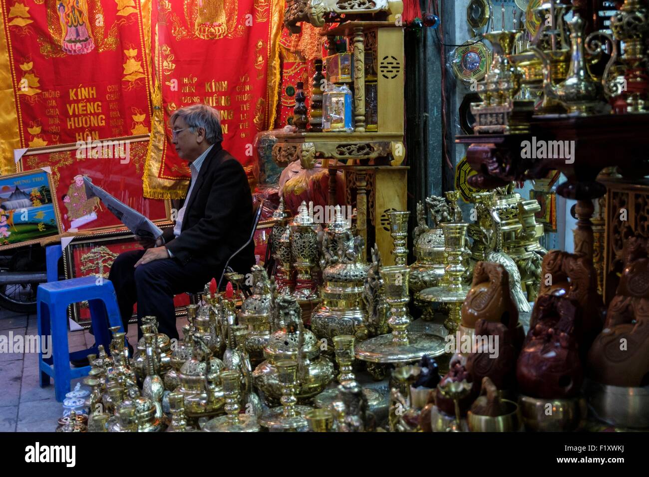 Vietnam, Hanoi, old city, a shopkeeper reading newspaper in front of ...