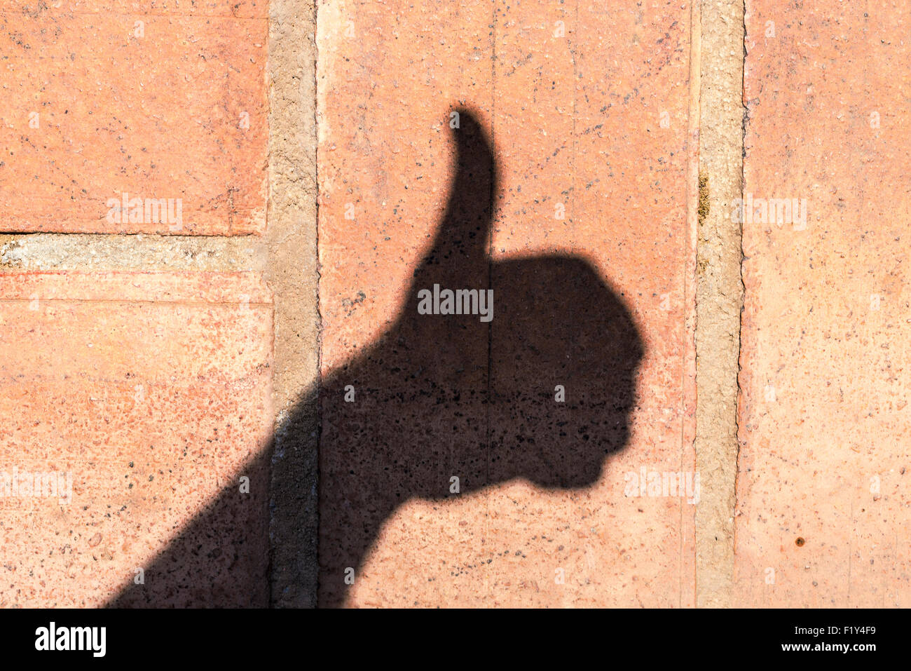 Shadow of a hand making the OK sign with thumb raised on a clay tile an ...