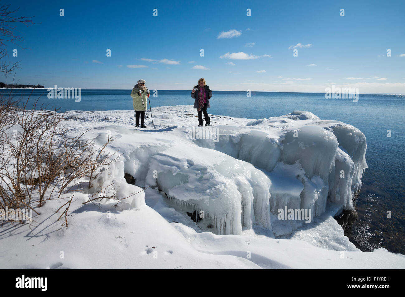 Two adult women explore a treacherous icy snowbank on the frozen shore ...