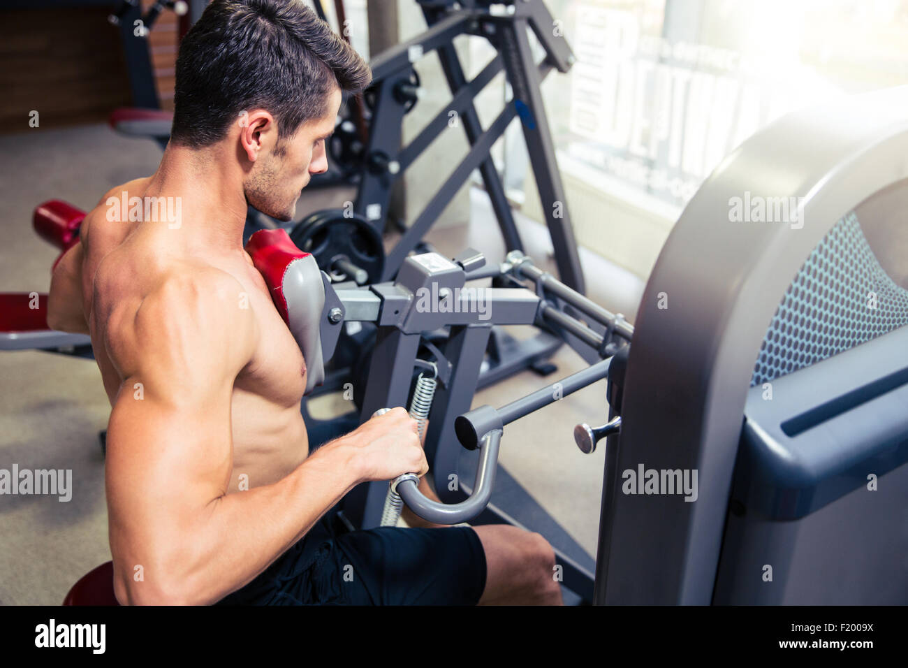 Portrait of a handsome man doing exercise on fitness machine in gym ...