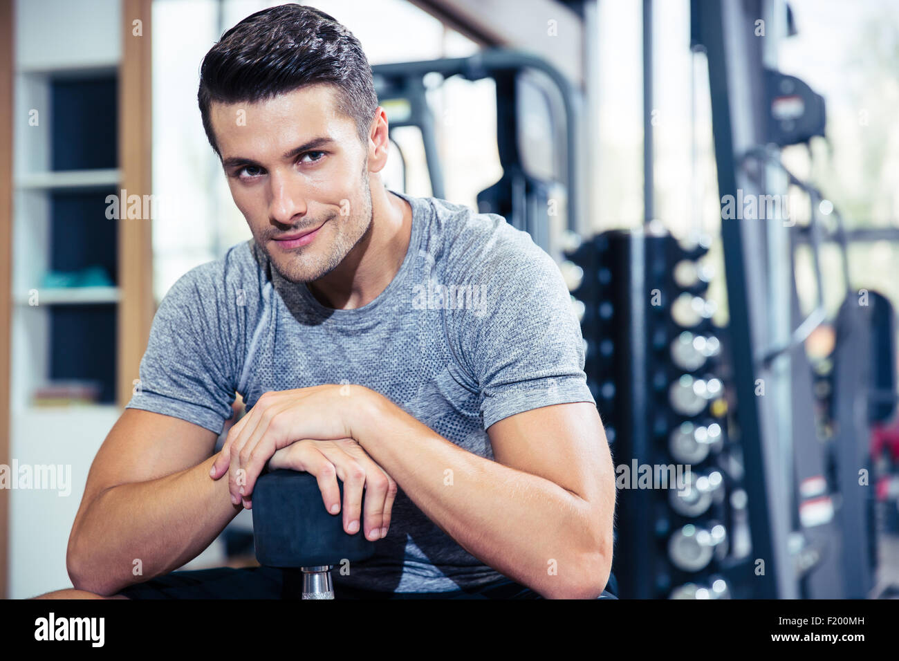 Portrait of a happy man sitting on the bench with dumbbells at gym ...
