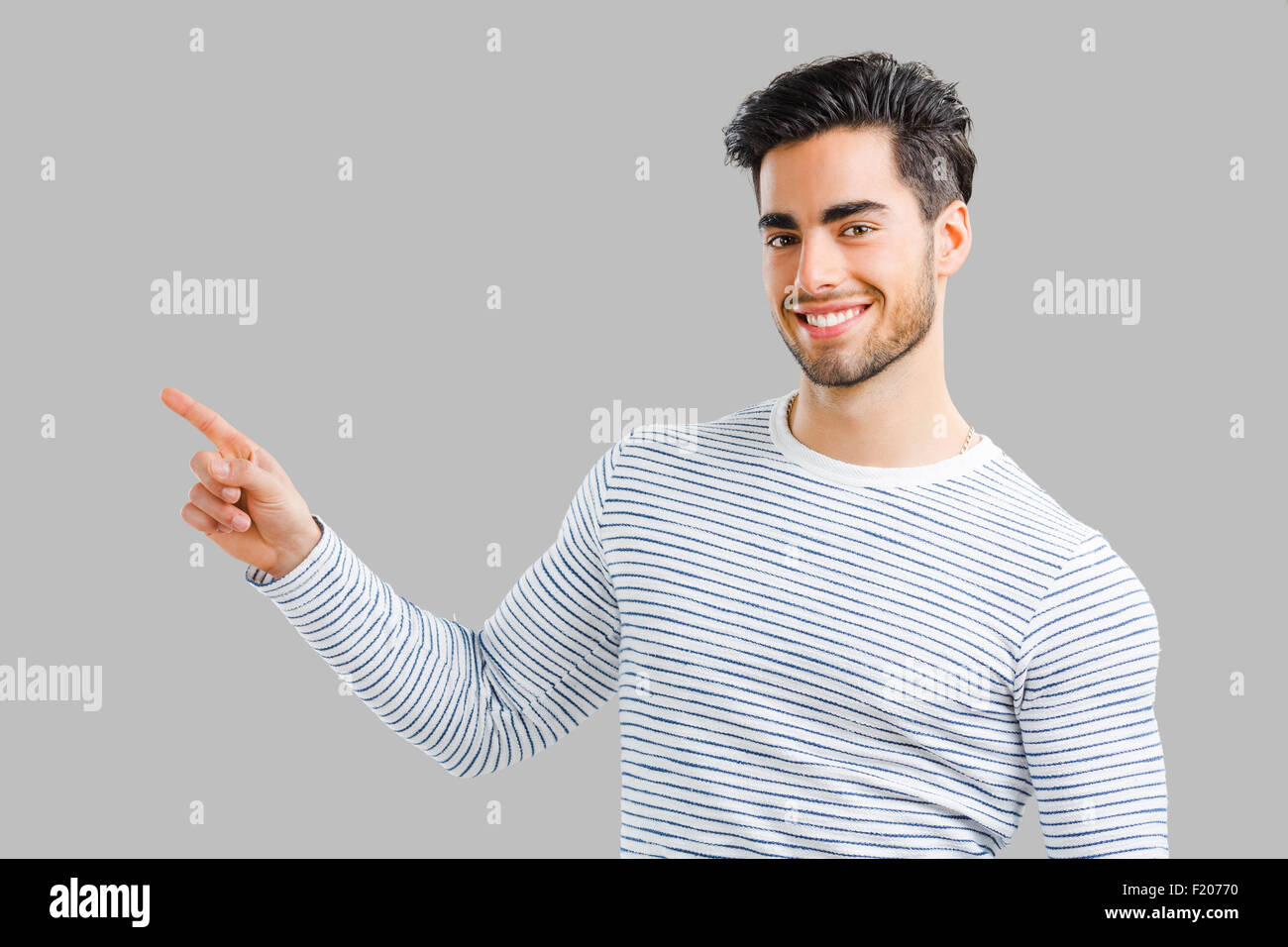 Handsome young man pointing with his right hand, isolated over gray ...