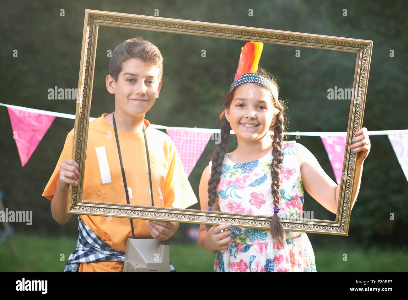 Boy and girl looking through picture frame, smiling, looking at camera ...