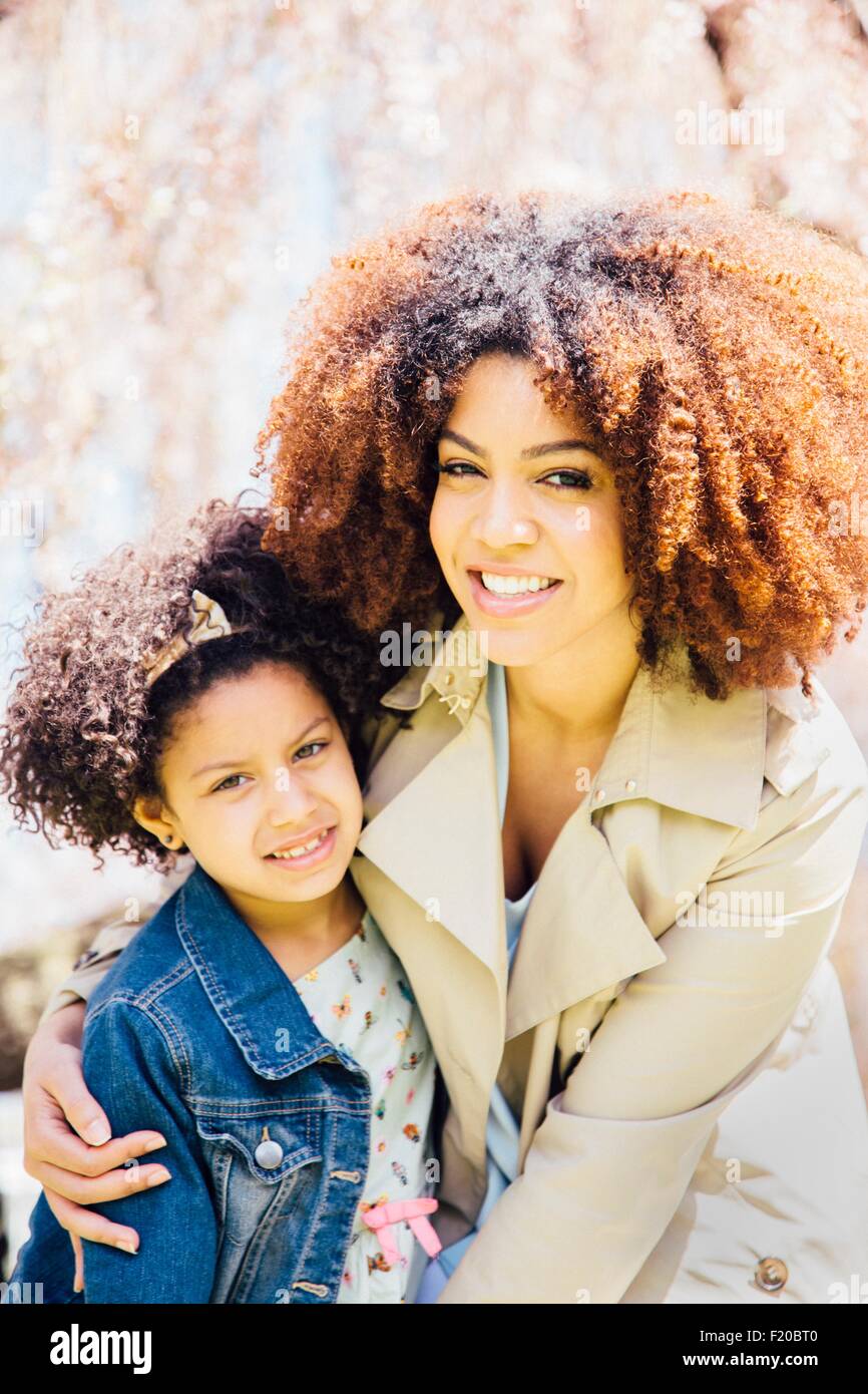 Portrait of mother with arm around daughter, looking at camera, smiling ...
