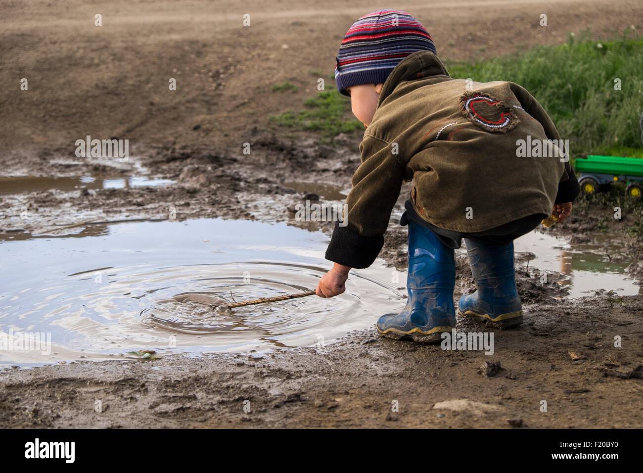 Male toddler wearing rubber boots playing with stick in puddle Stock ...