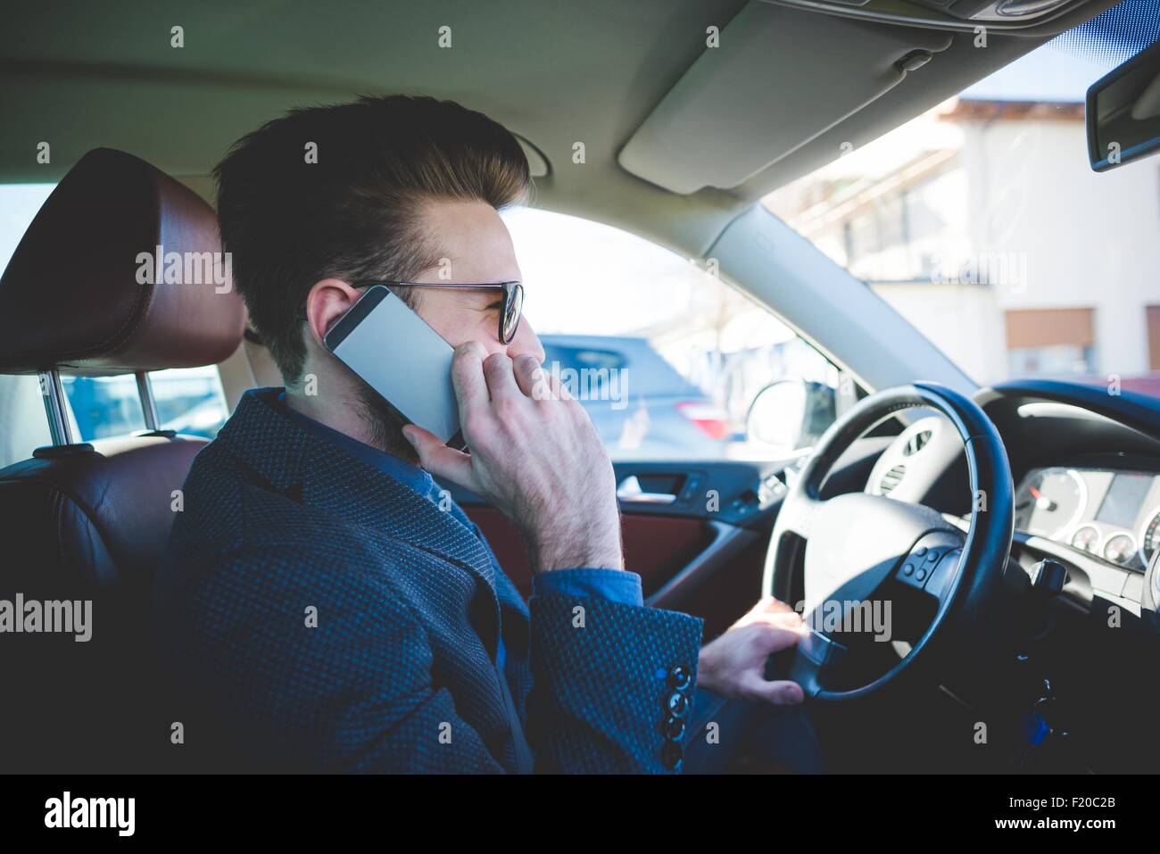 Stylish young man talking on smartphone whilst driving car Stock Photo ...