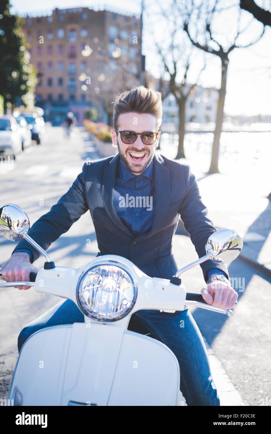 Portrait of smiling young man sitting on moped at roadside Stock Photo ...