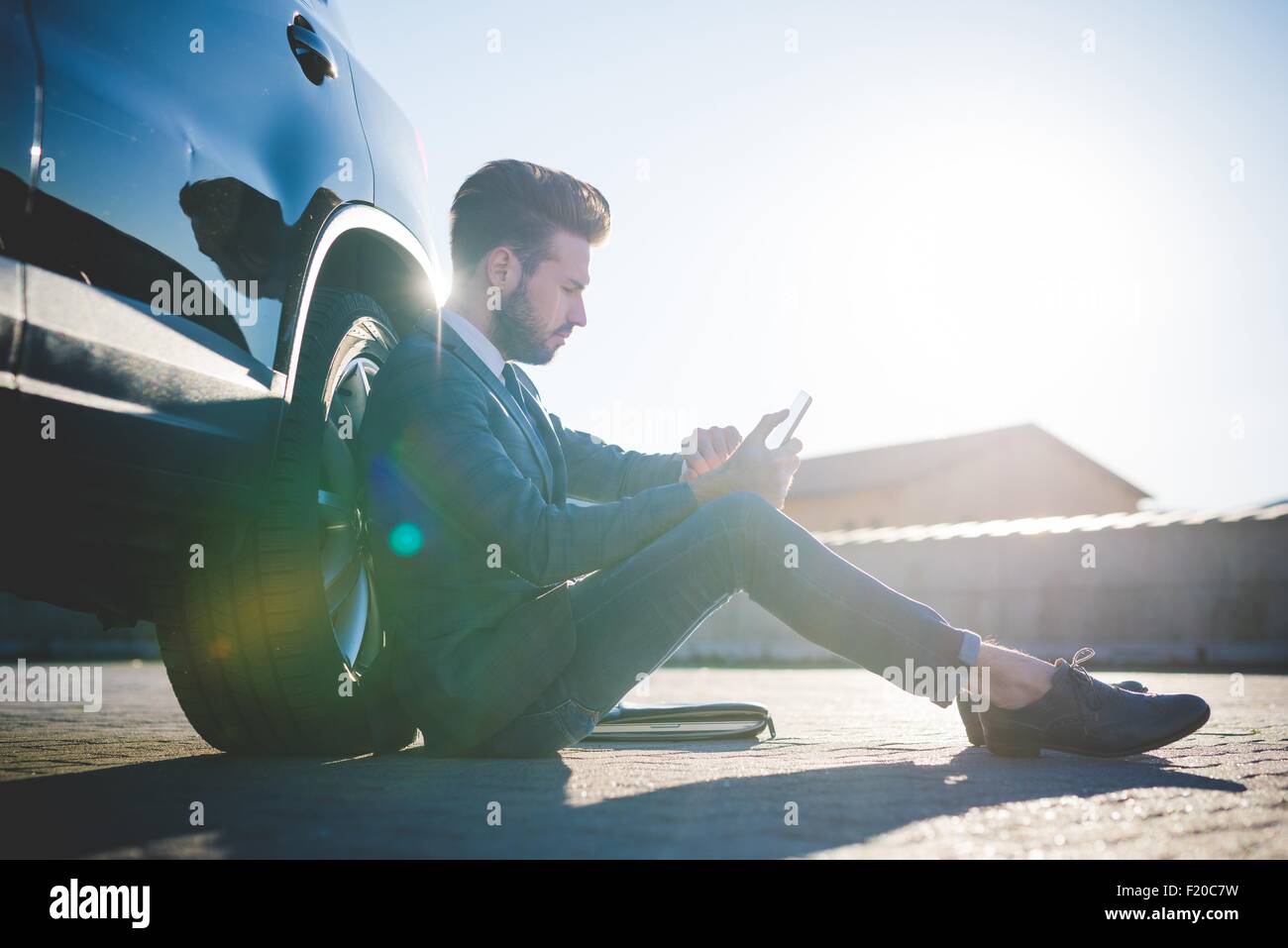 Stylish young man sitting leaning against car using digital tablet ...