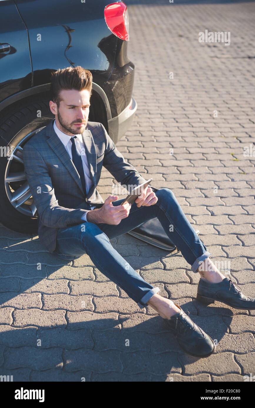 Stylish young man sitting leaning against car with digital tablet Stock ...