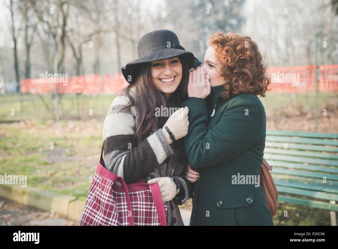 Two female adult friends whispering in park Stock Photo - Alamy