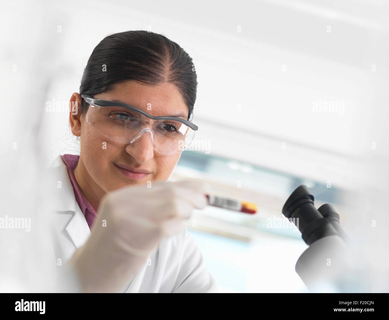 Young woman scientist viewing blood sample during clinical testing of ...