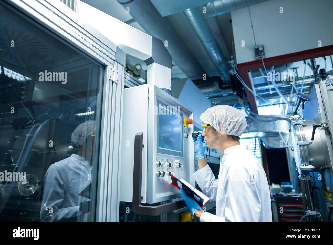 Male scientist with notebook adjusting control panel in lab cleanroom ...