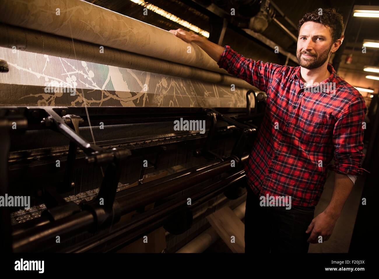 Portrait of male weaver next to old weaving machine in textile mill ...