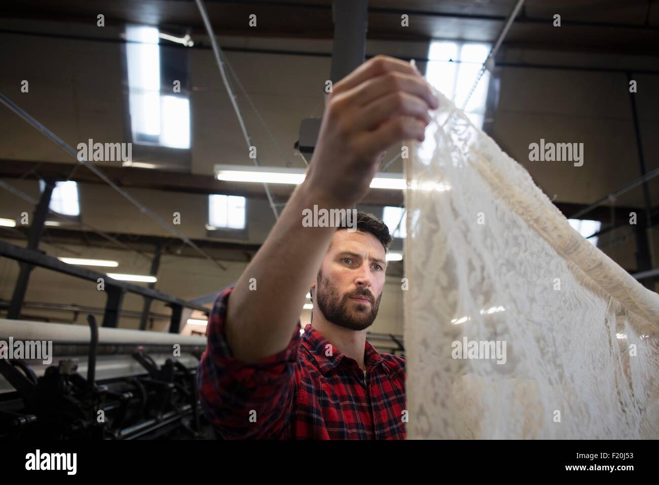 Portrait of male weaver examining lace cloth from old weaving machine ...