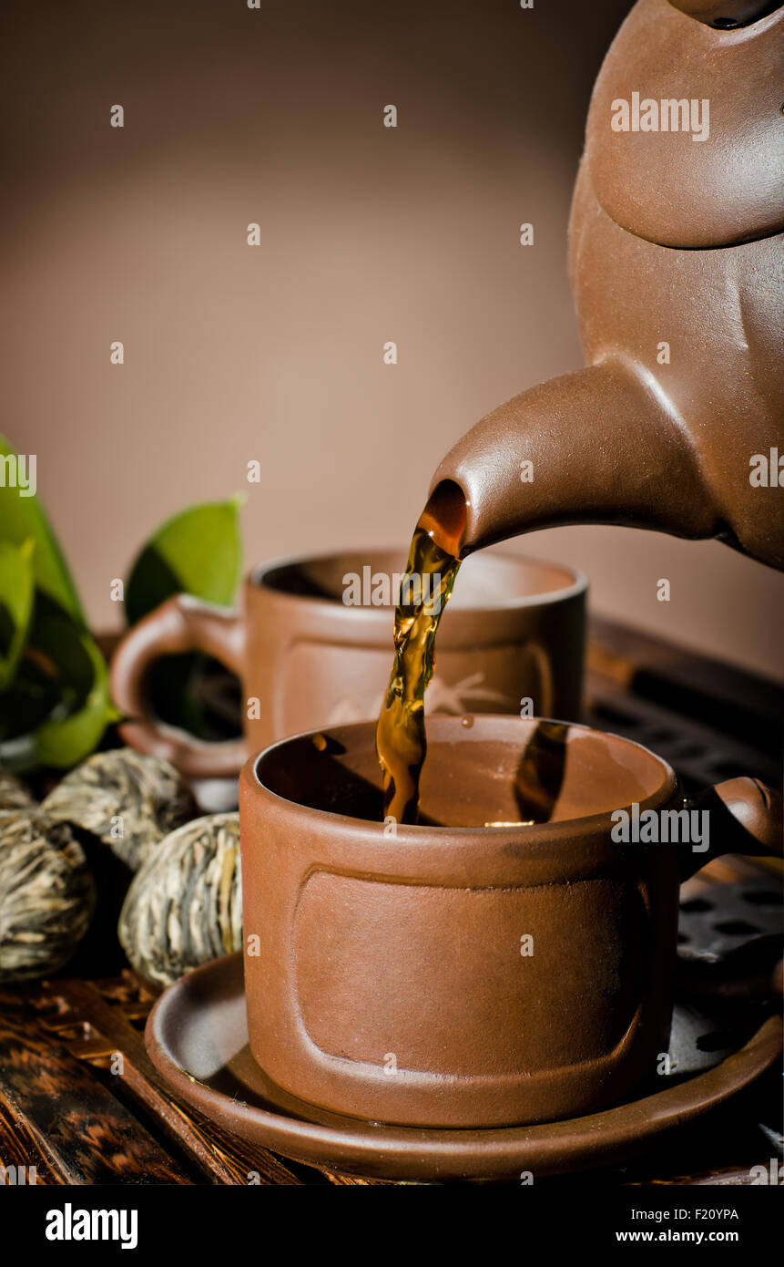 vertical photo, of the clay teapot tea flow in cup on brown background ...