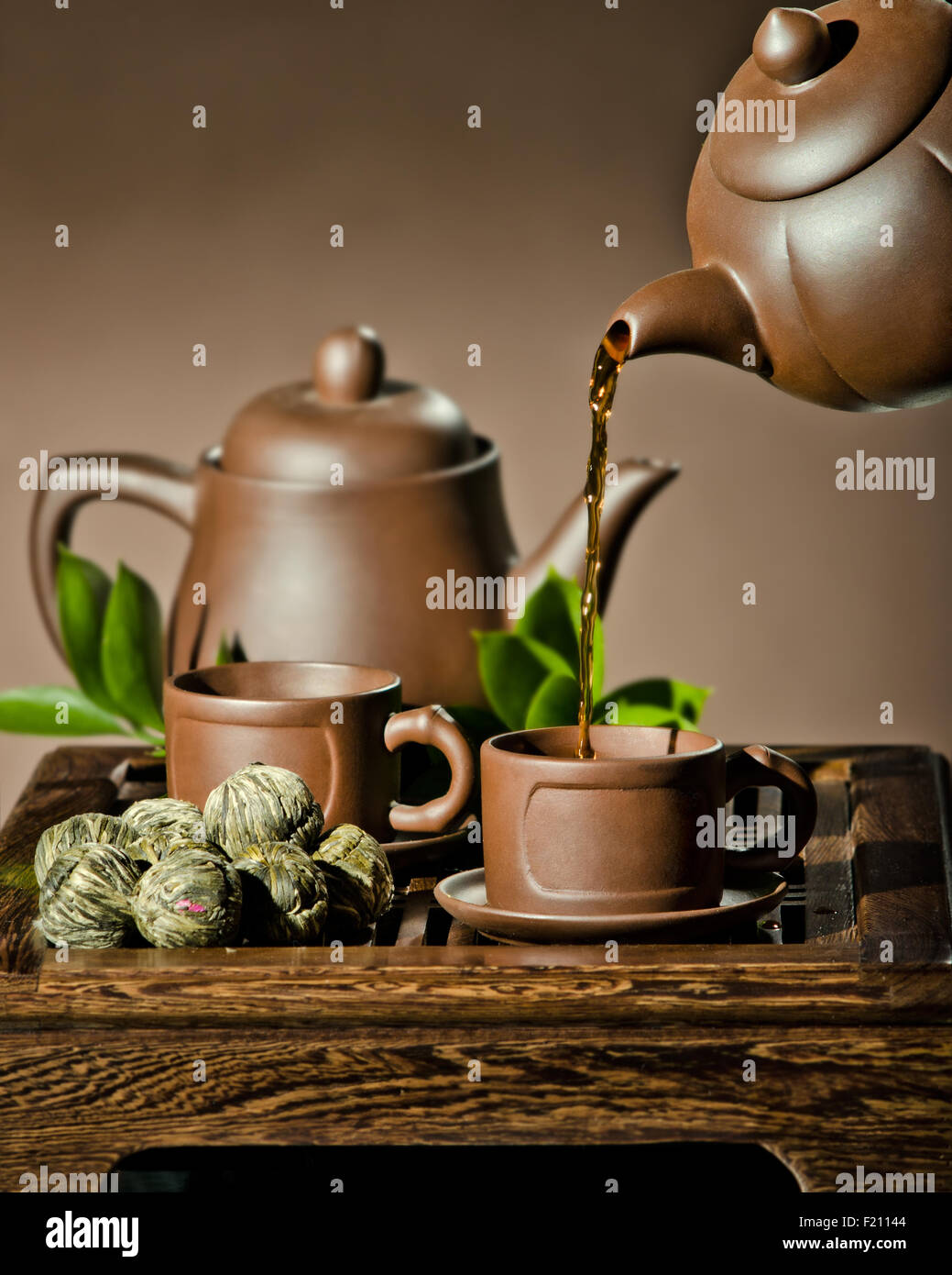 vertical photo, of the clay teapot tea flow in cup on brown background ...