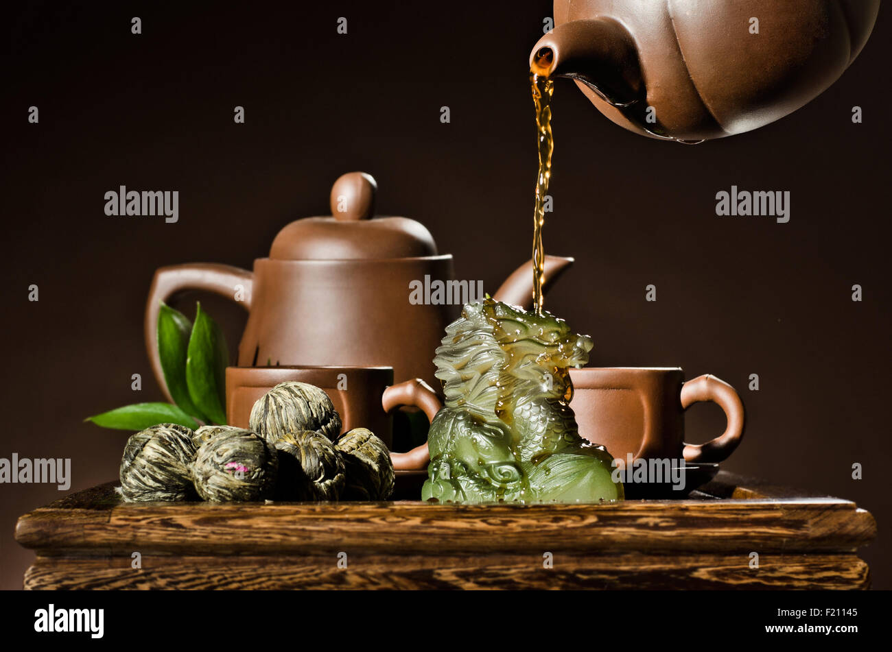vertical photo, of the clay teapot tea flow in cup on brown background ...