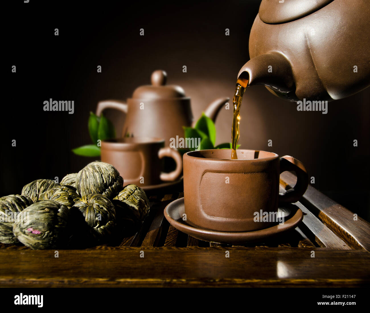 vertical photo, of the clay teapot tea flow in cup on brown background ...