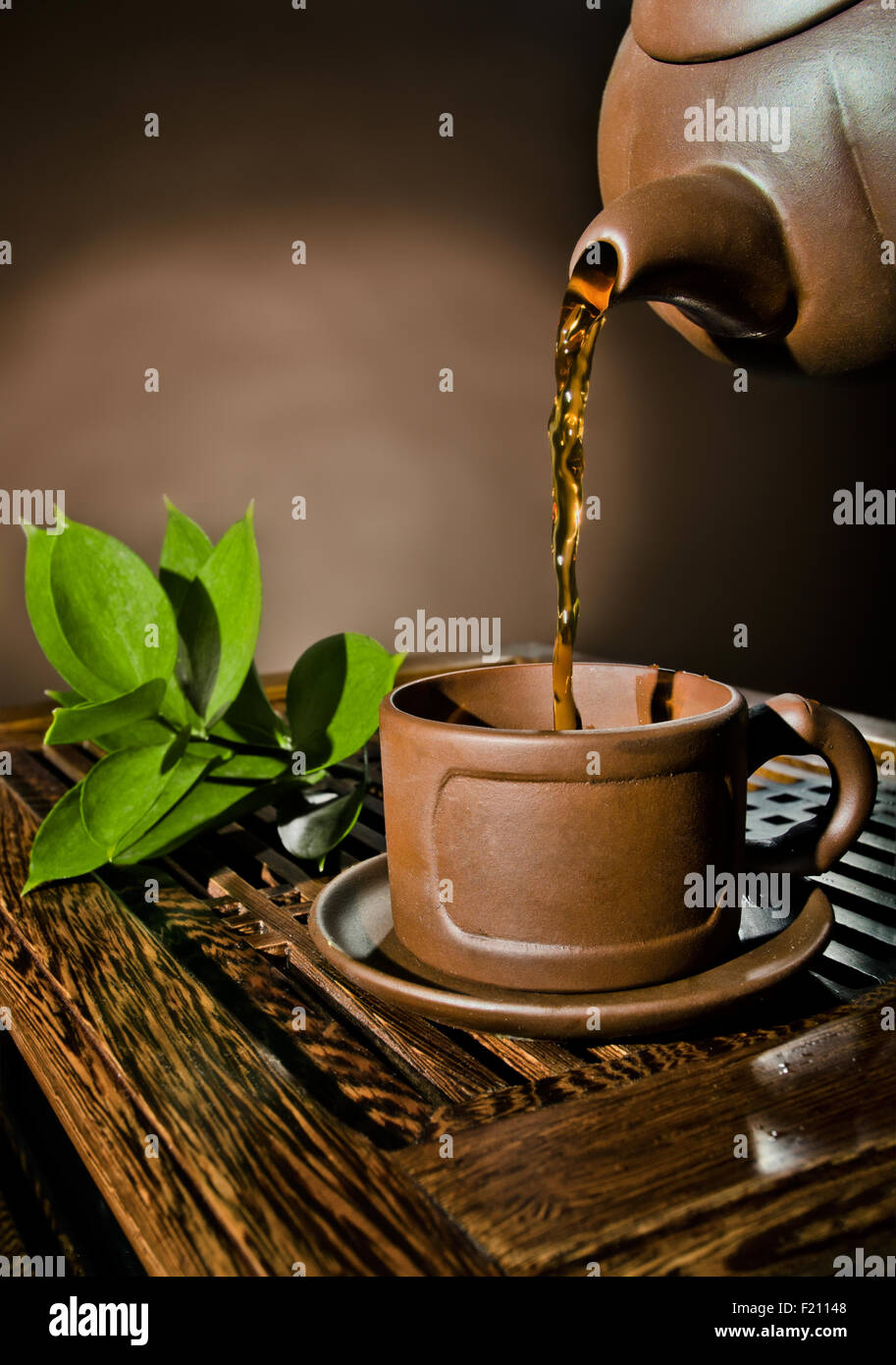vertical photo, of the clay teapot tea flow in cup on brown background ...