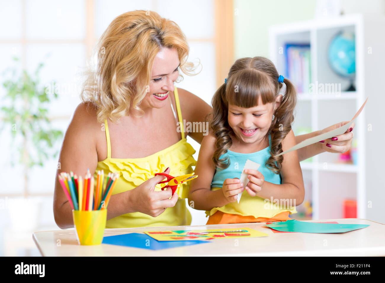 Child with woman cutting out scissors paper in preschool Stock Photo ...