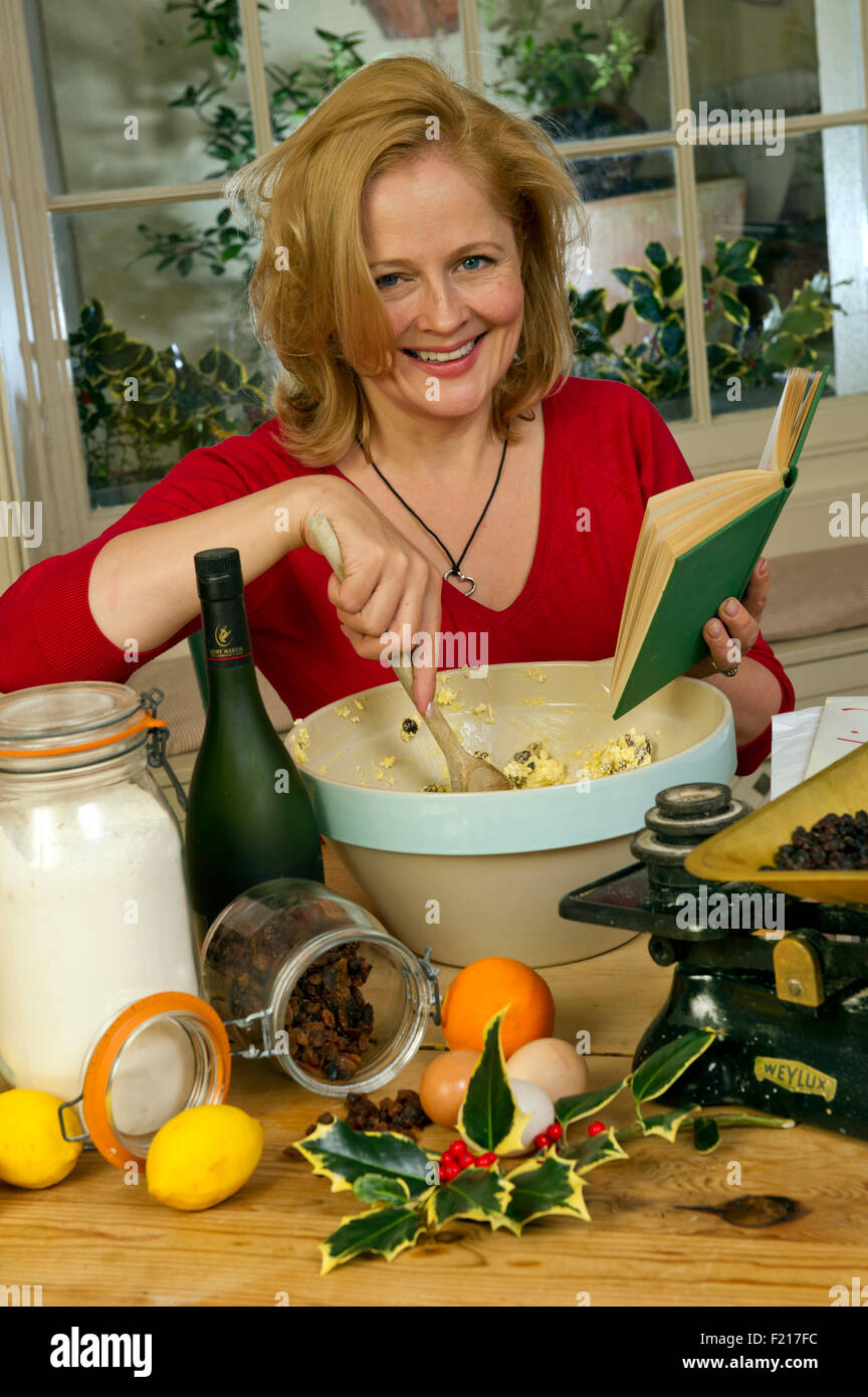 A woman in red mixing a Christmas pudding in a large bowl, using a ...