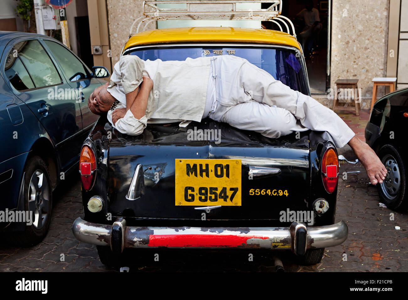 India, Maharashtra, Mumbai, Taxi driver fast asleep on the boot of his ...