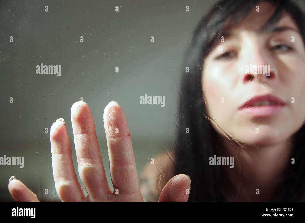 Beautiful sad young girl behind glass reaching out Stock Photo - Alamy