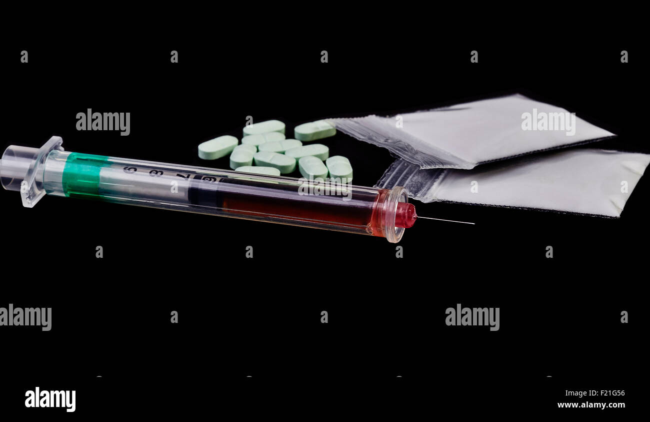 Heroin in a hypodermic needle with packets of heroin powder and pills ...