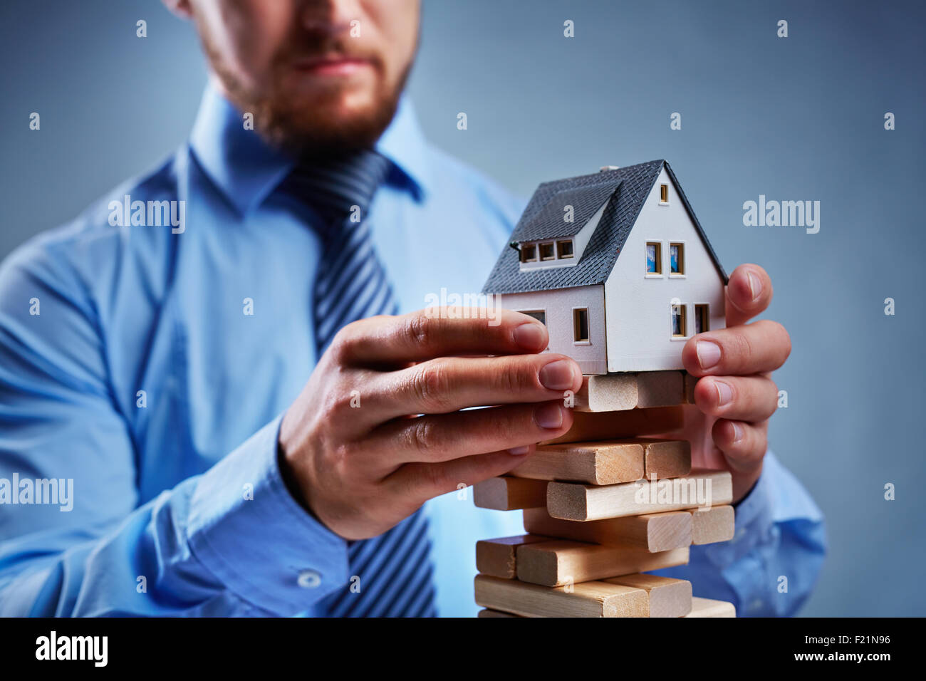 Businessman putting house model on top of tower from small wooden ...