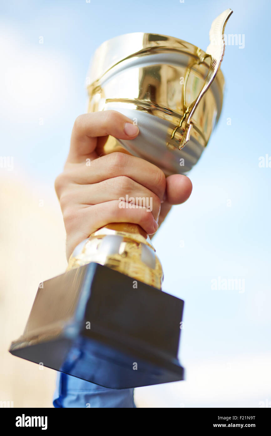 Human hand holding gold cup of winner Stock Photo - Alamy