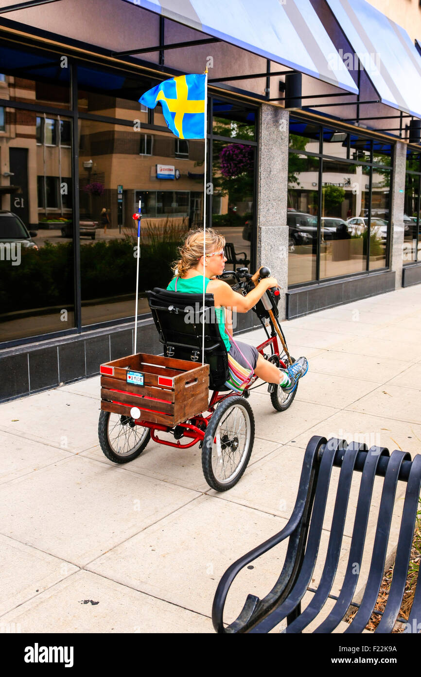 Adult woman riding her tricycle with a Swedish flag pennant on the back ...