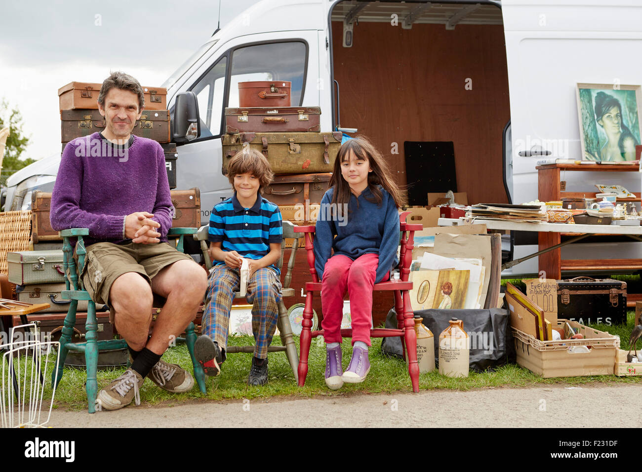 Man, boy and girl with trunks and baskets and furniture at flea market ...