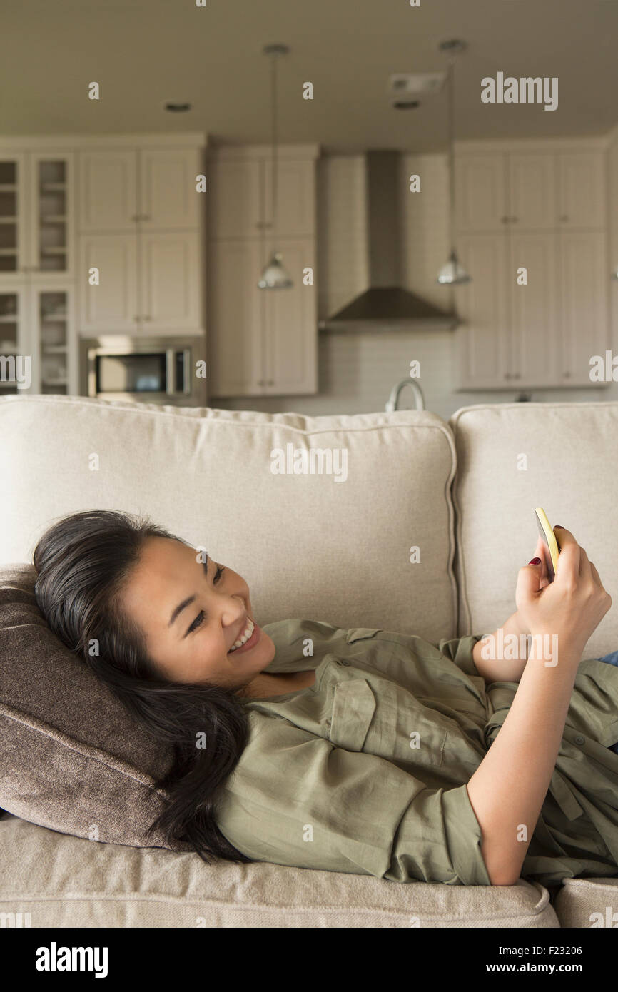 Woman lying on a sofa, smiling, looking at a cell phone Stock Photo - Alamy