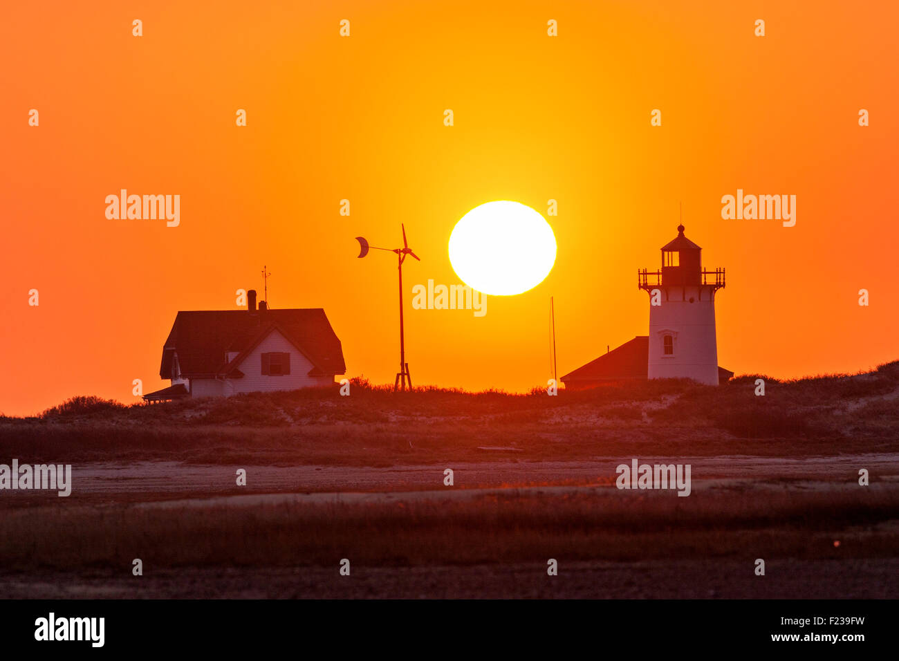 A lighthouse on the beach, a windmill turbine and a sunset Stock Photo ...