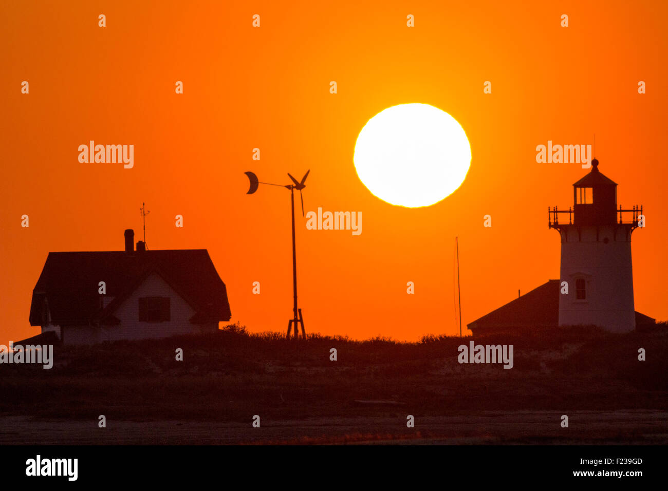 A lighthouse on the beach, a windmill turbine and a sunset Stock Photo ...