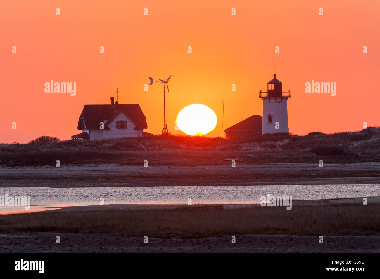 A lighthouse on the beach, a windmill turbine and a sunset Stock Photo ...