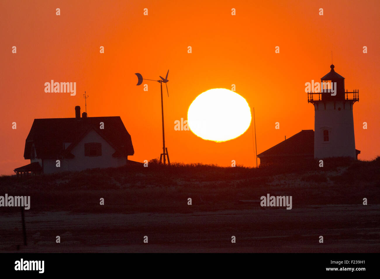 A lighthouse on the beach, a windmill turbine and a sunset Stock Photo ...