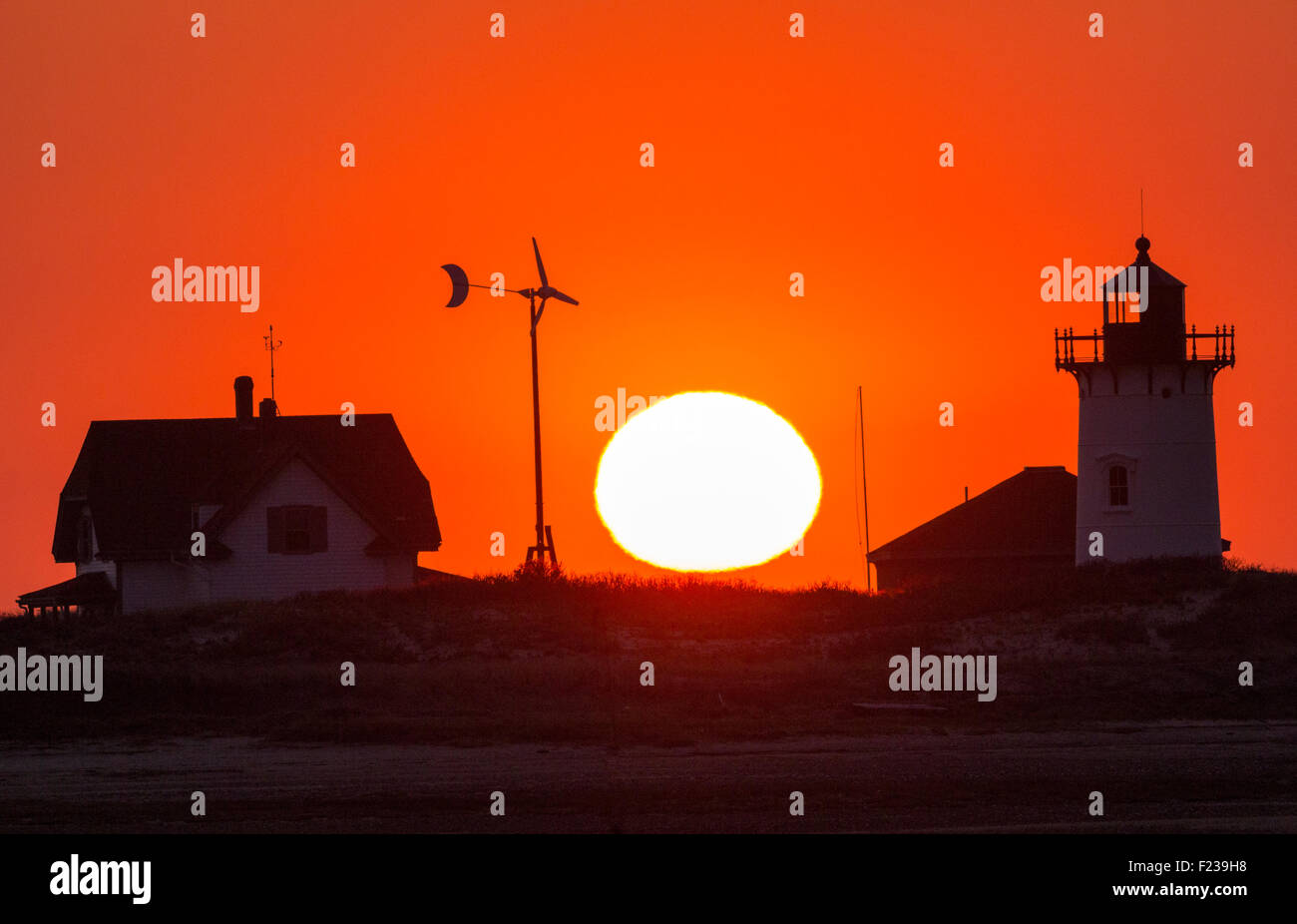 A lighthouse on the beach, a windmill turbine and a sunset Stock Photo ...