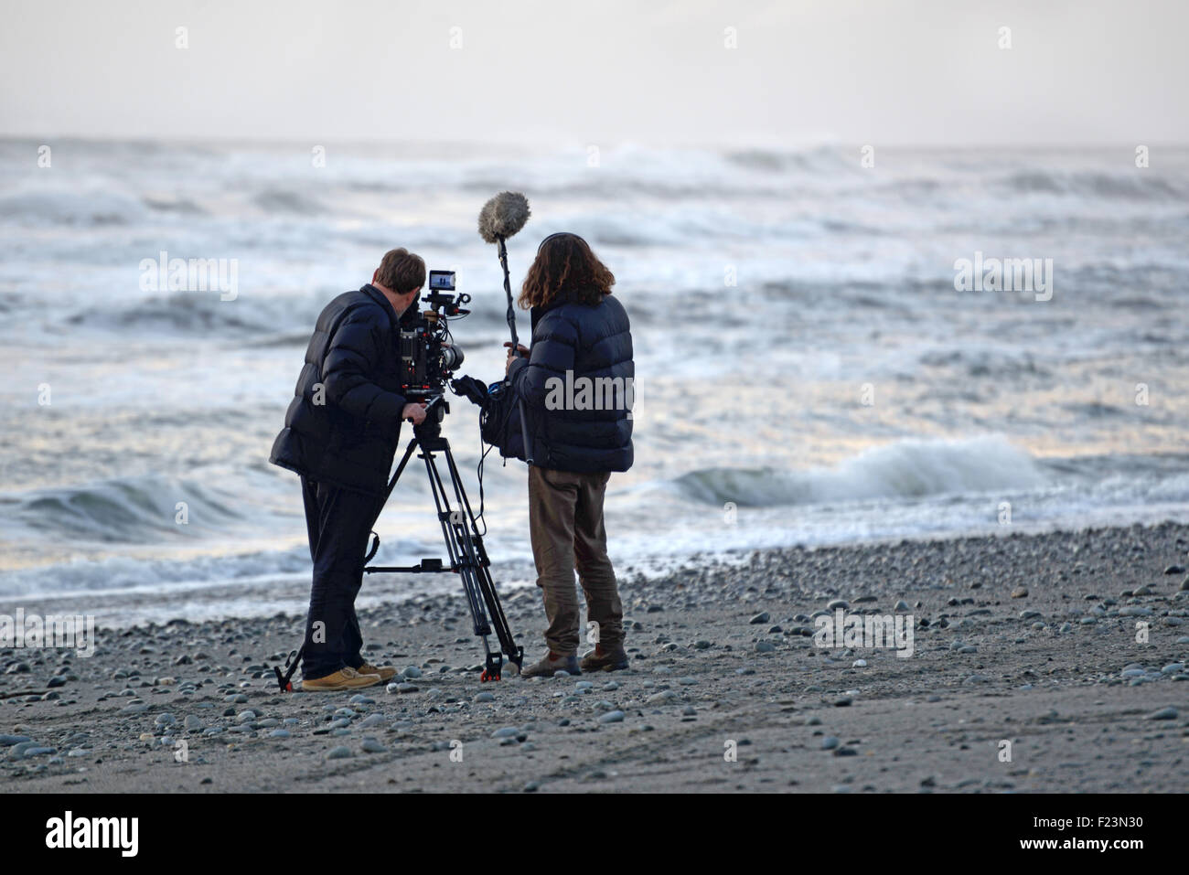 cameraman and sound recordist at work on a New Zealand beach at sunset ...