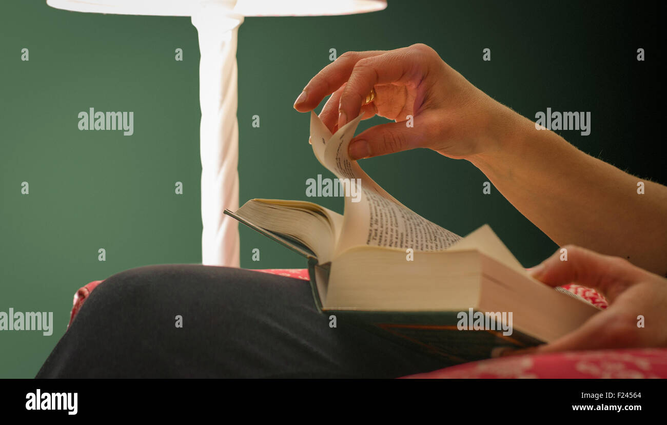 Woman hand holding and turning a page of a book, under light of lamp ...