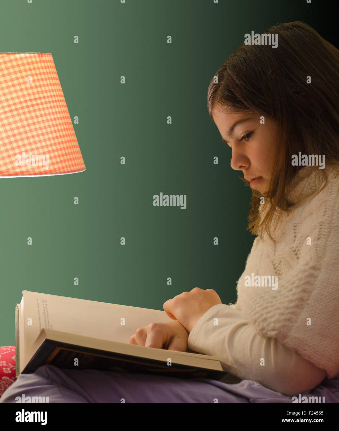 Little girl reading a book, under light of pink lamp, with green ...