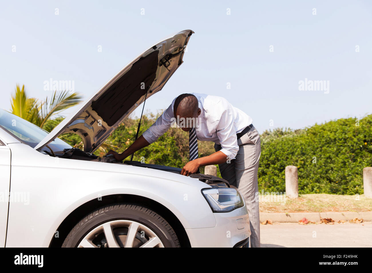 afro American man looking at broken down car engine by side of the road ...