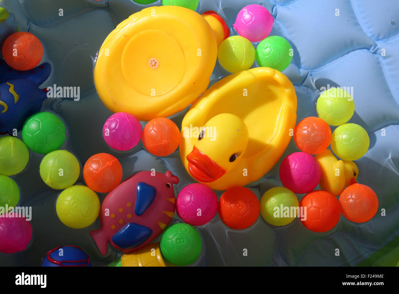 A yellow baby duck toy floating in water along with colorful balls in a ...