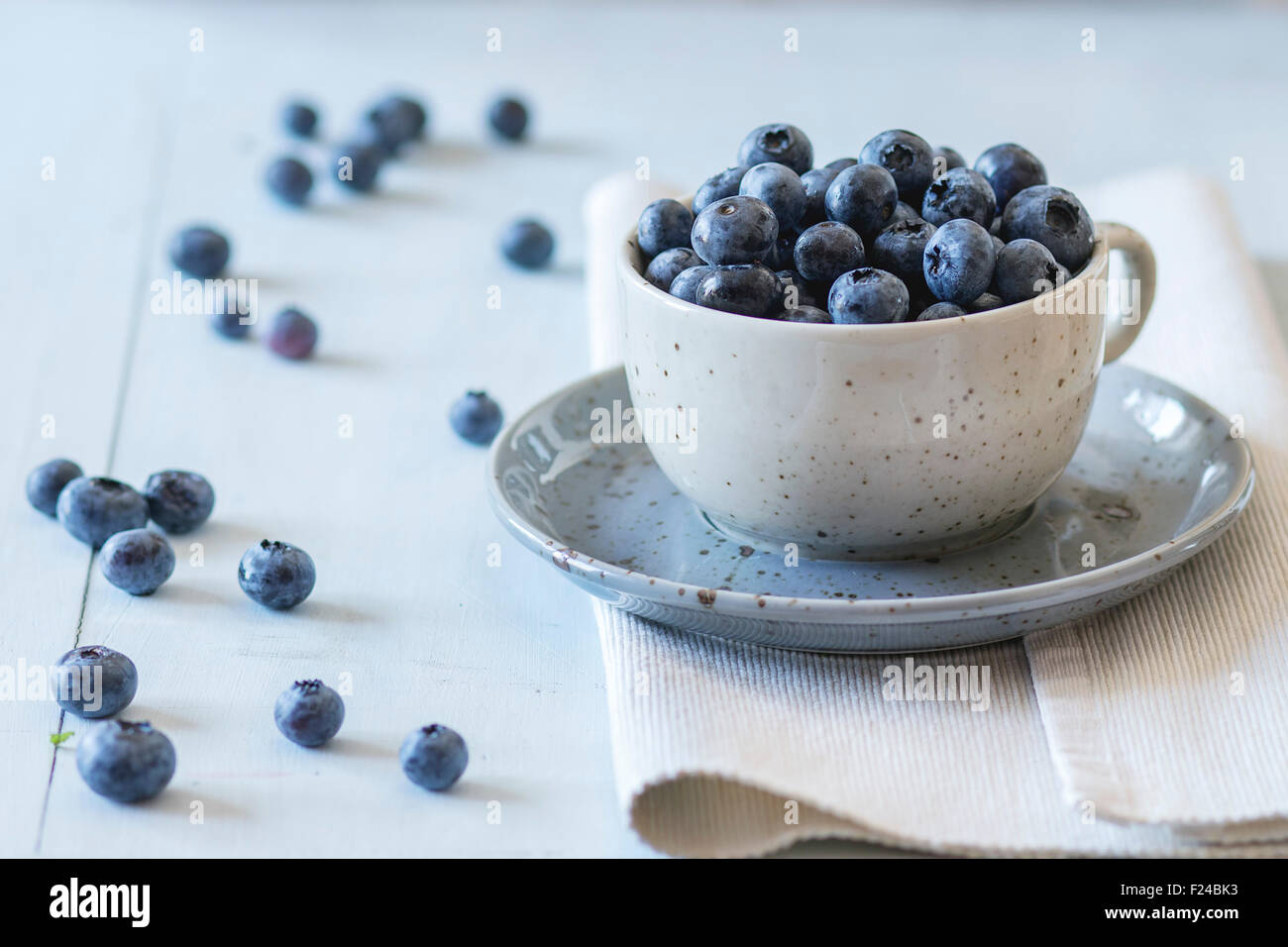 Spotted blue ceramic cup of blueberries with saucer at white textile ...