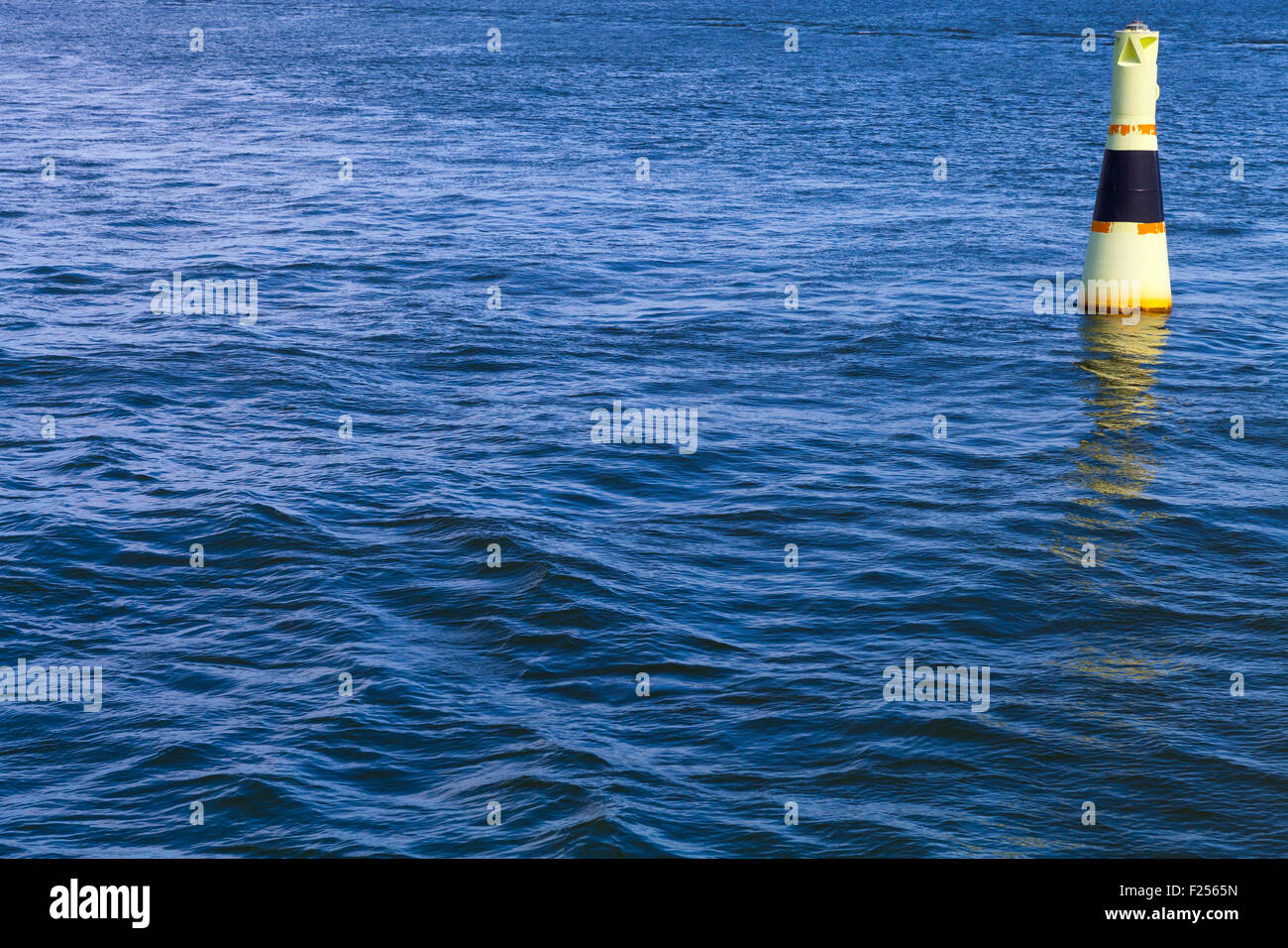 Yellow modern navigation buoy with black stripe floating on a sea water ...
