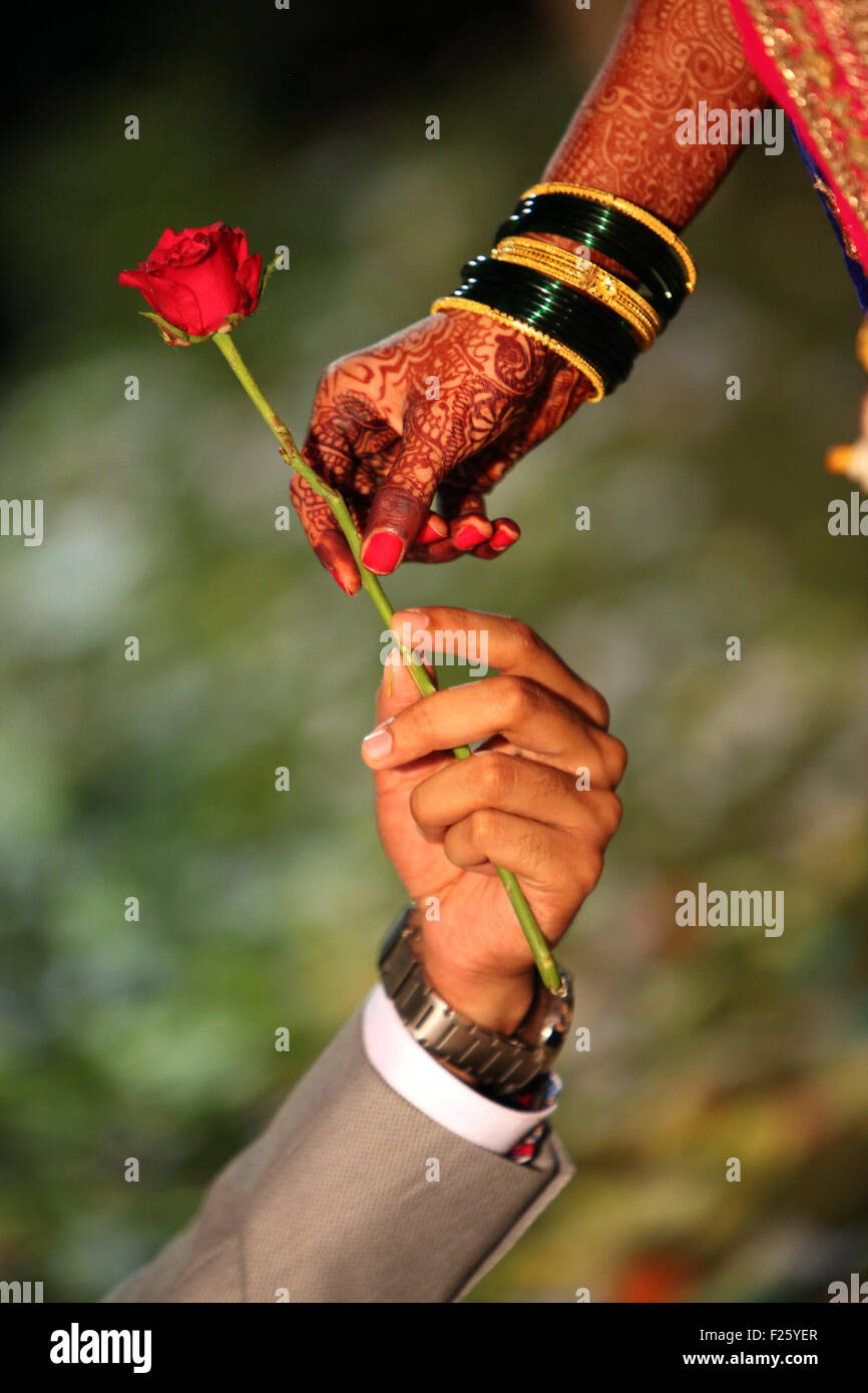 A groom offering a red rose to his bride whose hand is beautifully ...