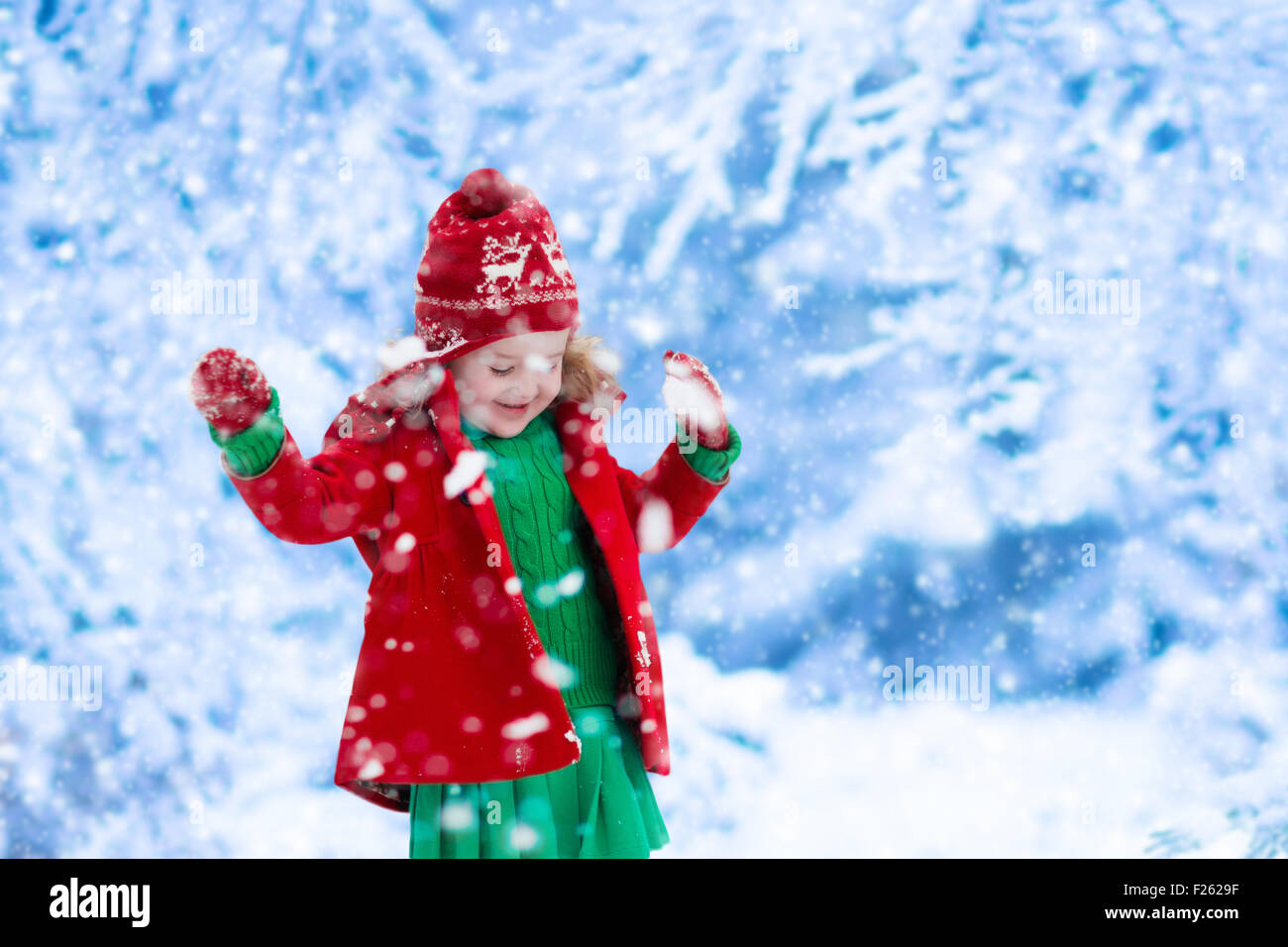 Little girl in red jacket and green knitted dress catching snowflakes ...