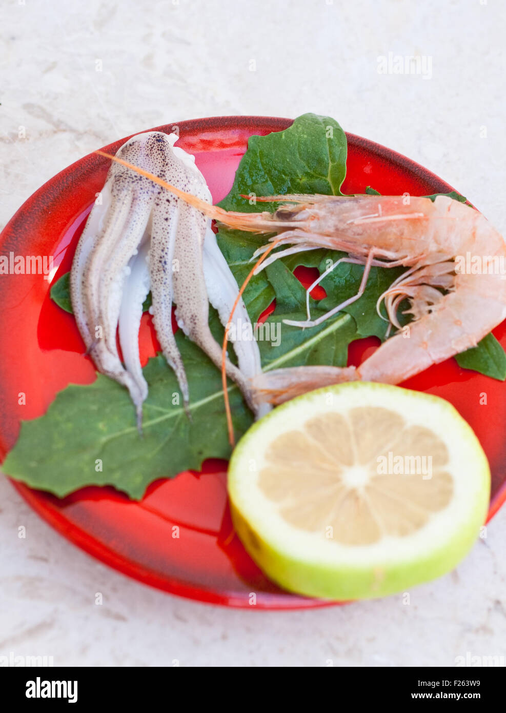 Shrimp, cuttlefish and lemon inside a red saucer Stock Photo - Alamy