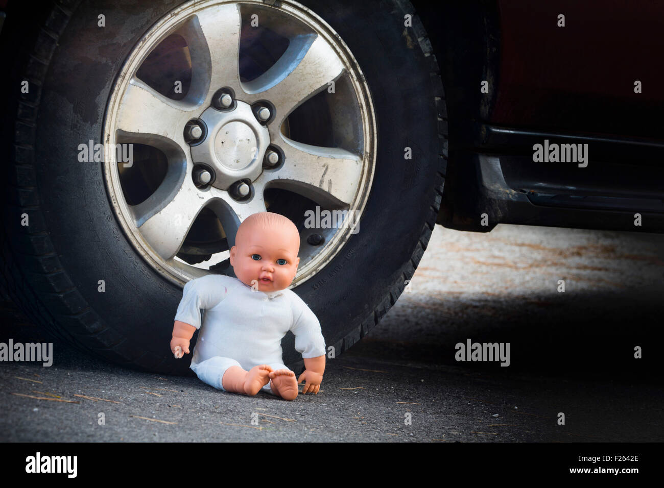 Baby doll sitting on road against wheel of vehicle Stock Photo - Alamy
